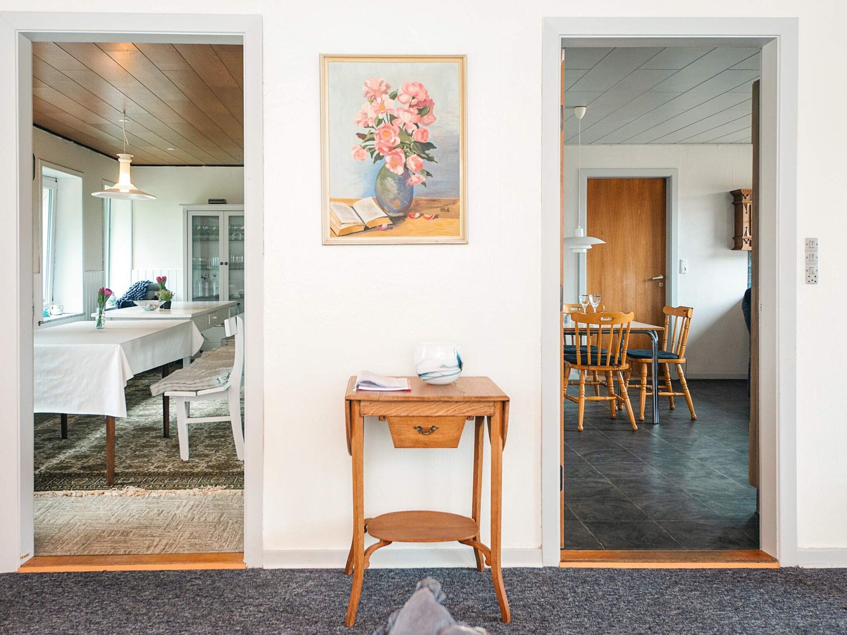 Quarto com área de jantar, mesa com um vaso de flores e um quadro na parede.