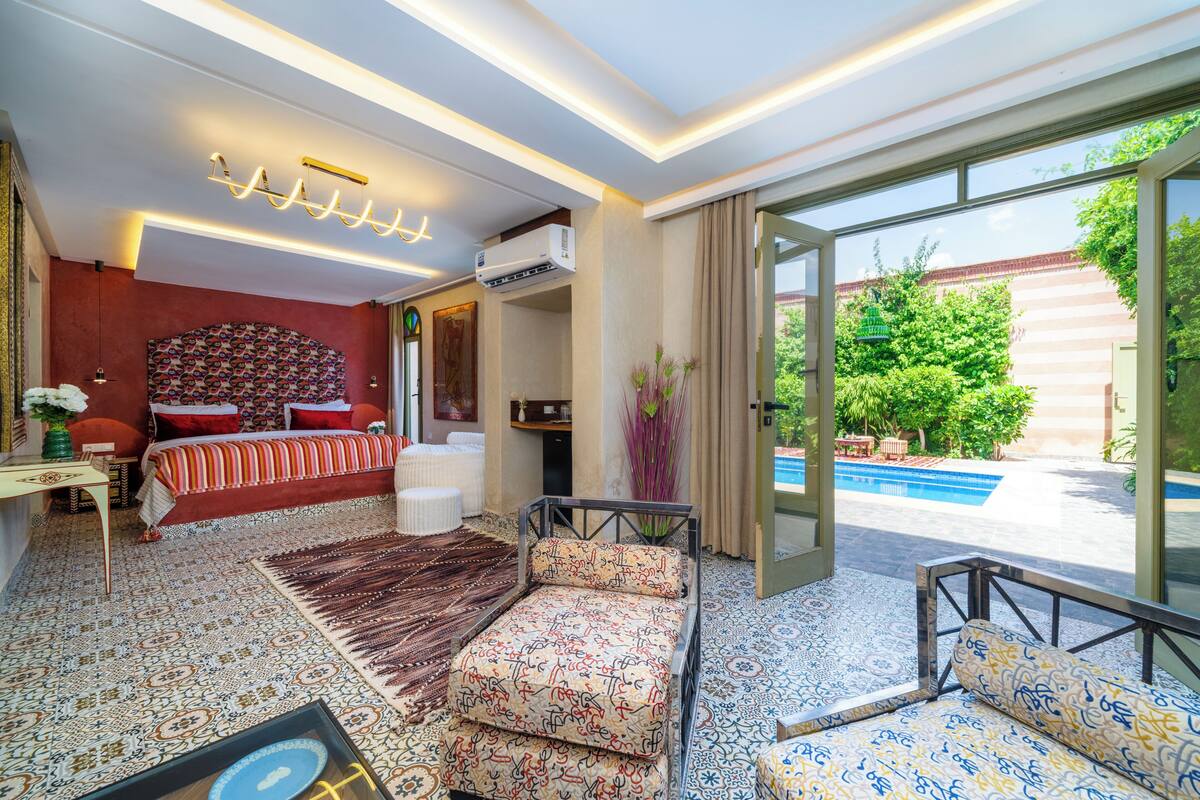 Quarto com cama, escrivaninha, cadeira, sofá e vista para uma piscina ao ar livre.