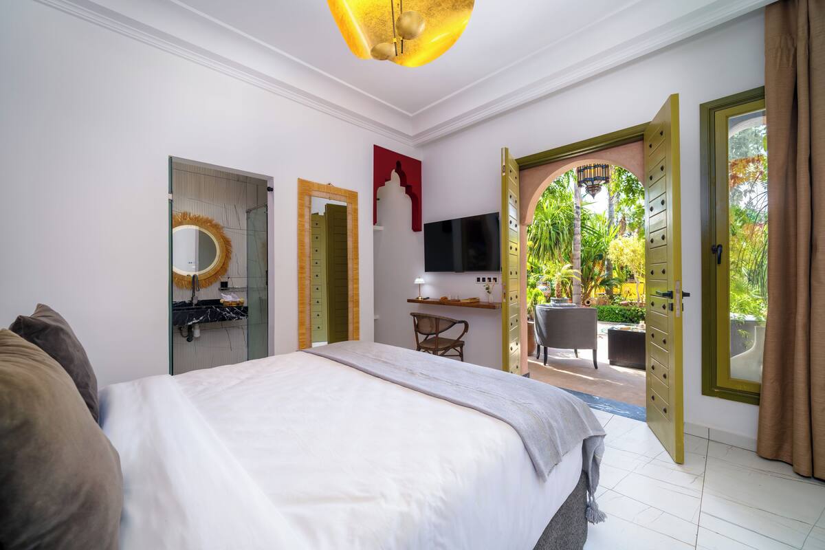 Quarto com cama, televisão, escrivaninha e vista para o exterior.