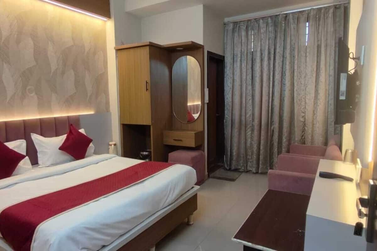 Quarto de hotel com cama, escrivaninha, espelho, guarda-roupa e banheiro com chuveiro.