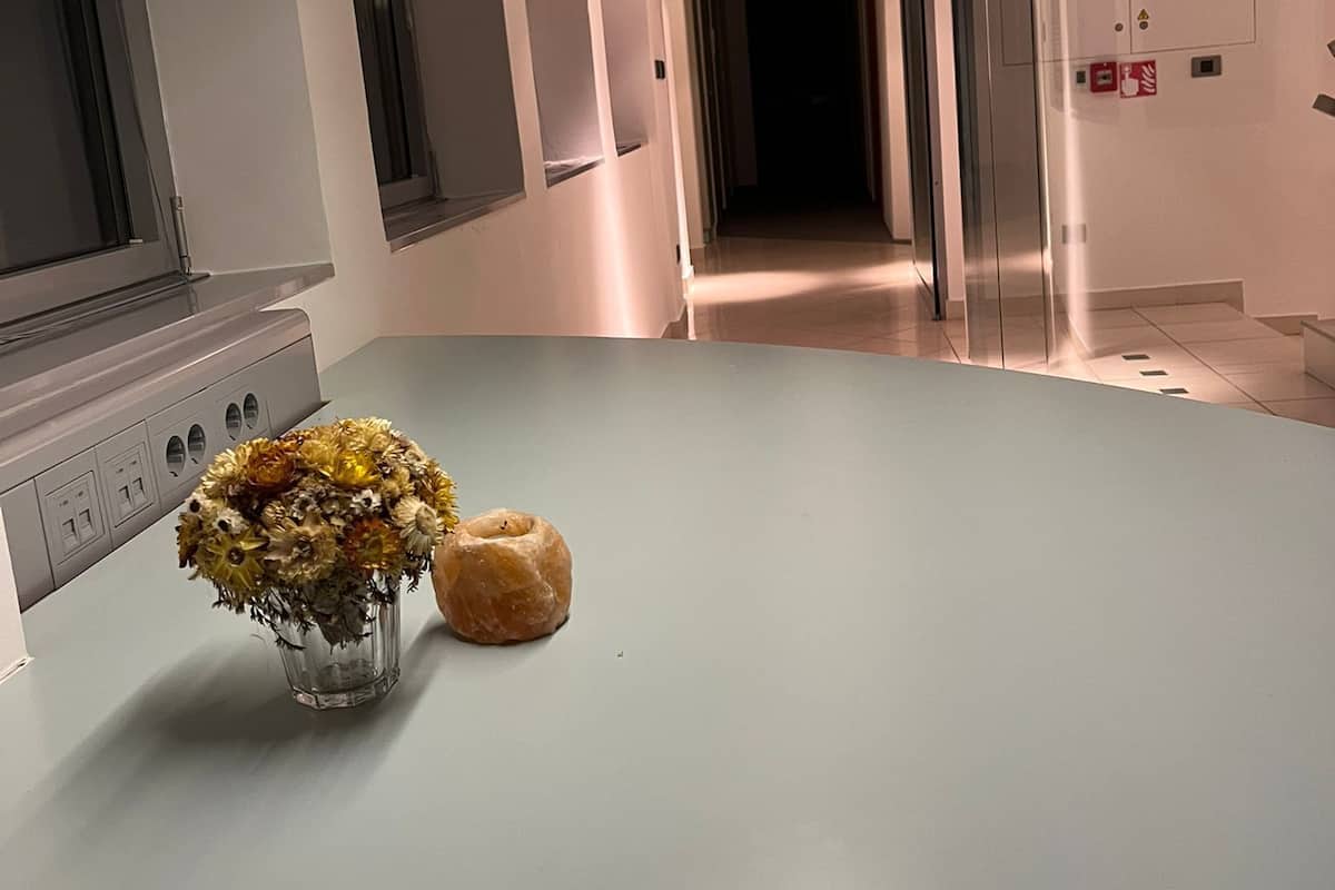 Um corredor com uma porta de vidro, um pequeno vaso com flores e um donut em cima de uma mesa.