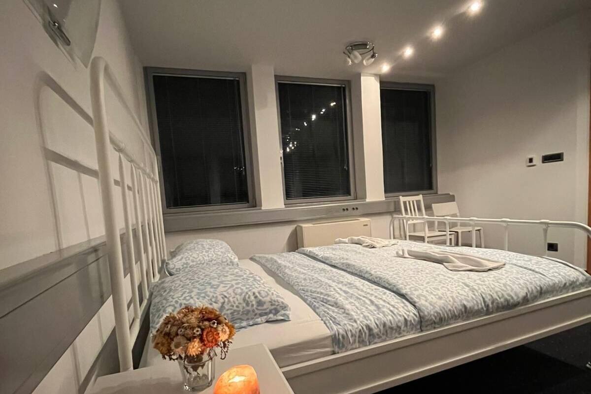 Quarto moderno com cama, mesa de cabeceira e um criado-mudo com um vaso e vela.