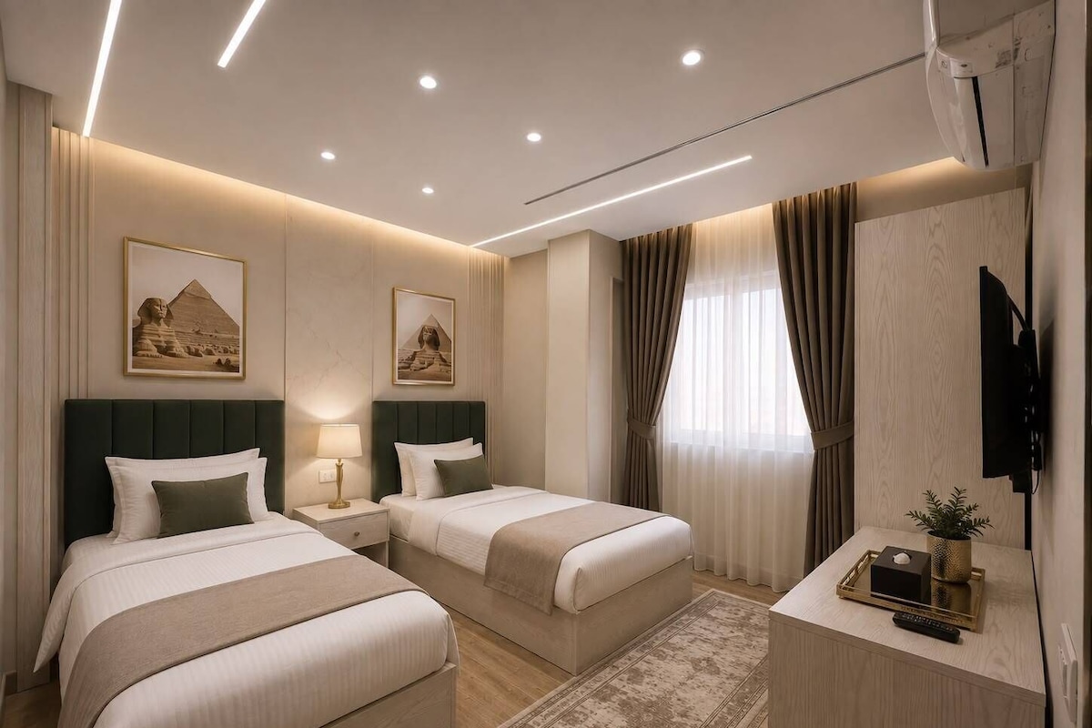 Quarto de hotel com duas camas, uma escrivaninha, televisão e obras de arte nas paredes.