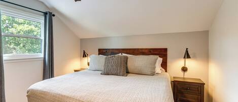 Quarto com cama, mesas de cabeceira, ventoinha no teto, janela e vista para árvores.