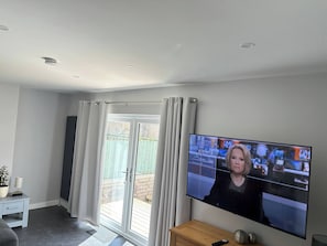 Uma sala de estar moderna com televisão, porta de vidro deslizante, uma mesinha e um vaso de planta.