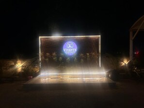 Vista noturna de um edifício com um letreiro iluminado chamativo que diz 'VIVANTE HOSPITALITY'.