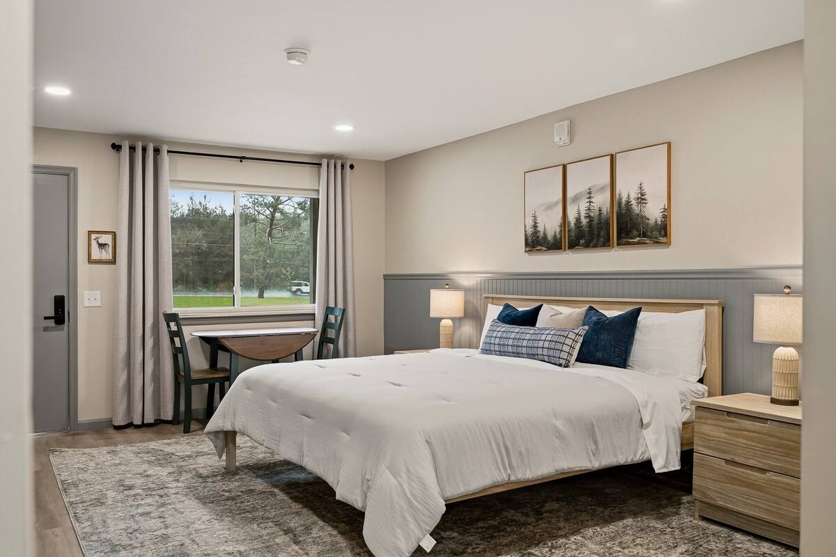 Quarto com uma cama grande, mesas de cabeceira, escrivaninha e janela com cortinas.