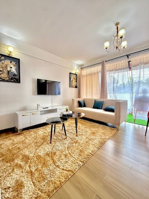 Uma sala de estar moderna com um sofá, uma televisão, um console branco e um tapete estampado.