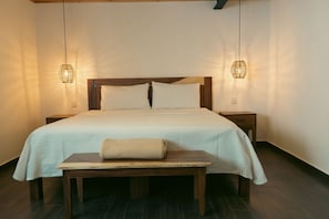 Quarto bem organizado com cama, mesas de cabeceira, um banco e luminárias pendentes.