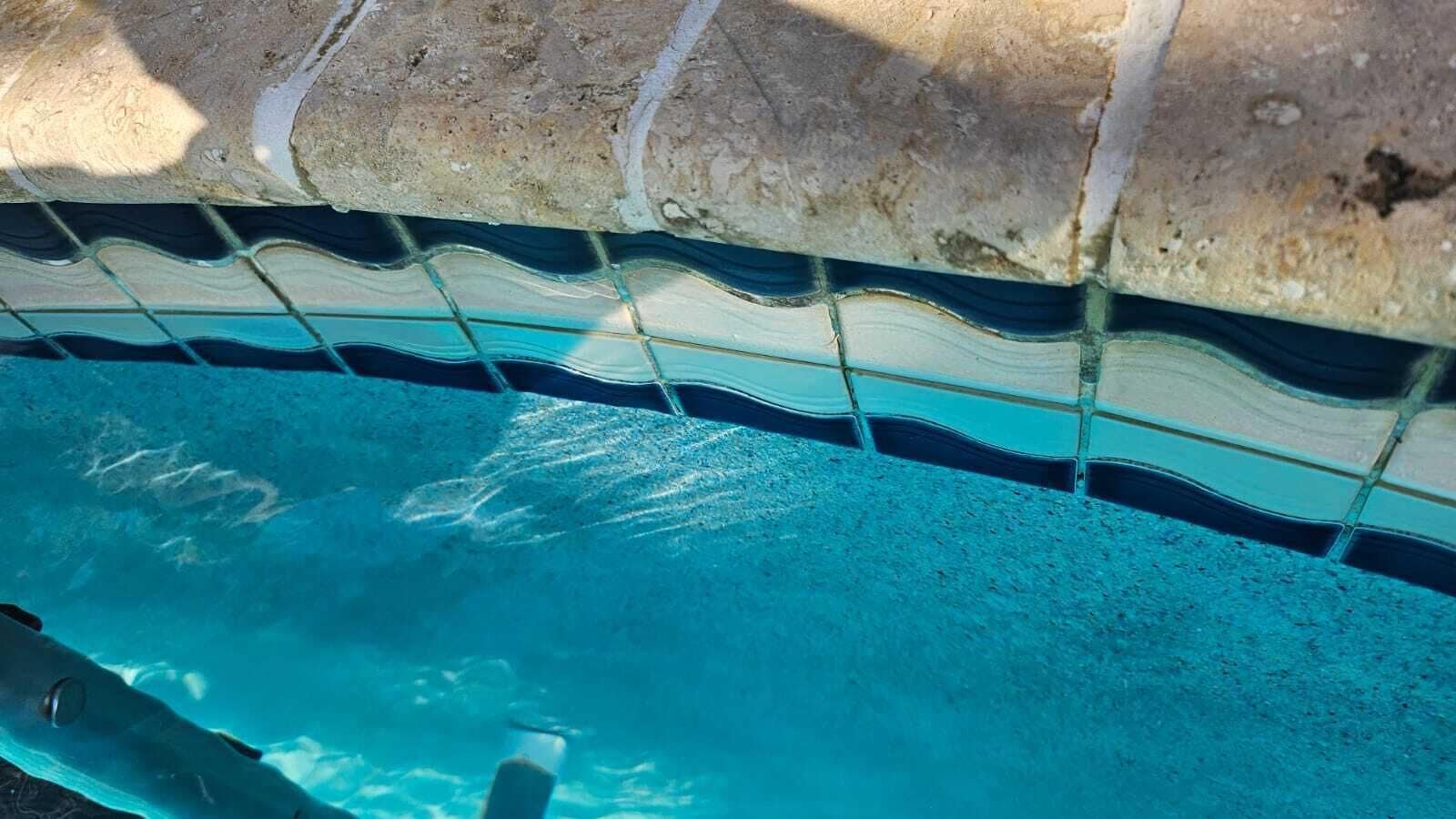 Piscina com águas azuis cristalinas, paredes azulejadas e um borde de pedra.