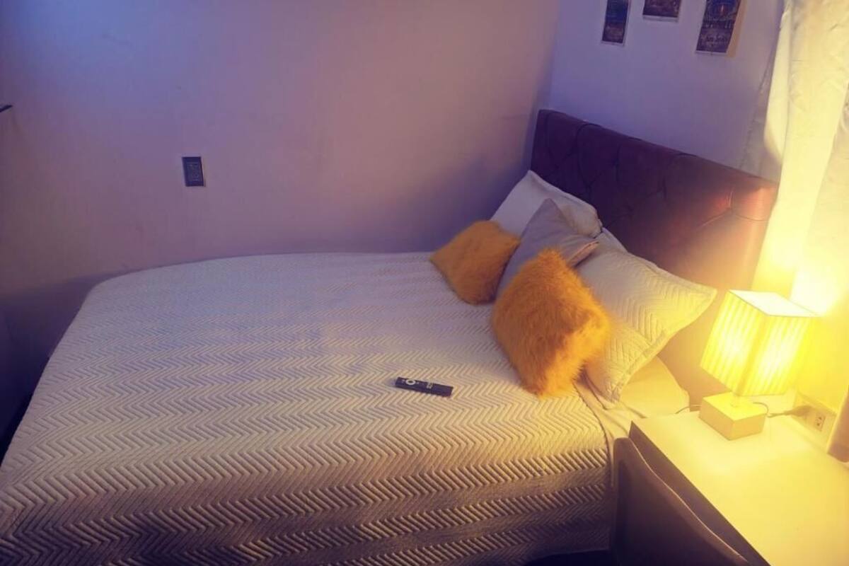 Uma cama bem arrumada com um cobre-leito estampado, um controle remoto e uma luminária de cabeceira.
