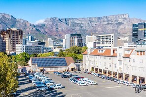 Um estacionamento com vários carros, um edifício com painéis solares e montanhas ao fundo.