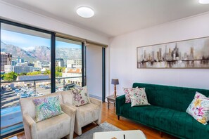 Uma sala de estar moderna com um sofá, duas poltronas, um quadro e vista para um horizonte urbano através de amplas janelas.