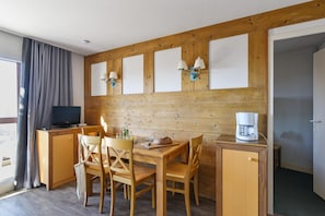 Quarto com parede de madeira, mesa com cadeiras, televisão, cafeteira e armário.