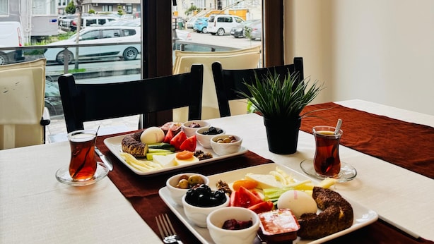 Uma mesa de jantar com uma refeição, um vaso de plantas e vista para prédios e carros pela janela.