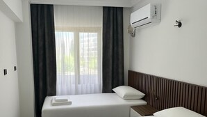 Quarto de hotel com duas camas, janela com cortinas, ar condicionado e luminária na parede.