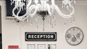 Balcão de recepção com lustre, relógio e placa indicativa da área.