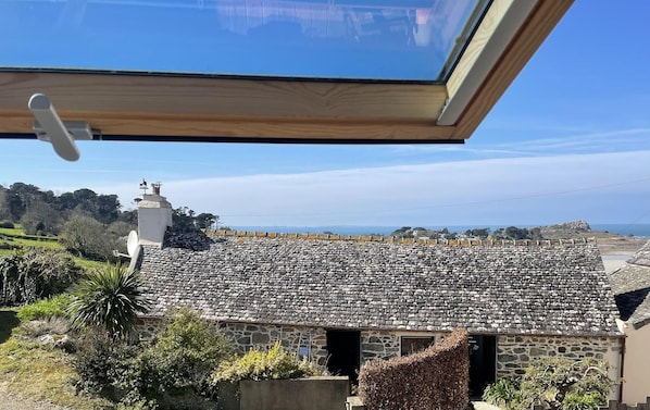 Um edifício de pedra com telhado em telhas, claraboia e vista da paisagem.