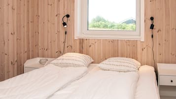 Quarto com parede de madeira, janela, cama com roupa de cama branca e abajures laterais.