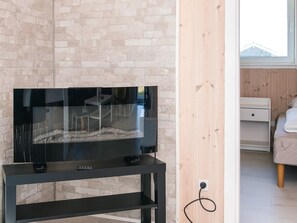 Quarto moderno com televisão sobre suporte preto, parede de madeira e cama com cabeceira branca.