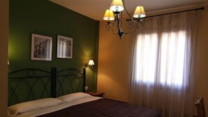 Quarto com cama, um lustre, duas molduras na parede e janela com cortinas.