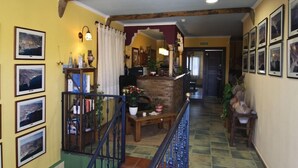 Um corredor com escada de madeira, balcão de recepção, quadros nas paredes e chão de azulejos.
