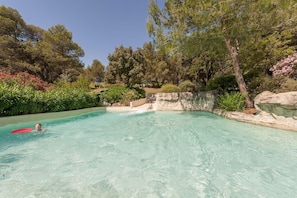 Piscina com água cristalina, cercada por vegetação e árvores.