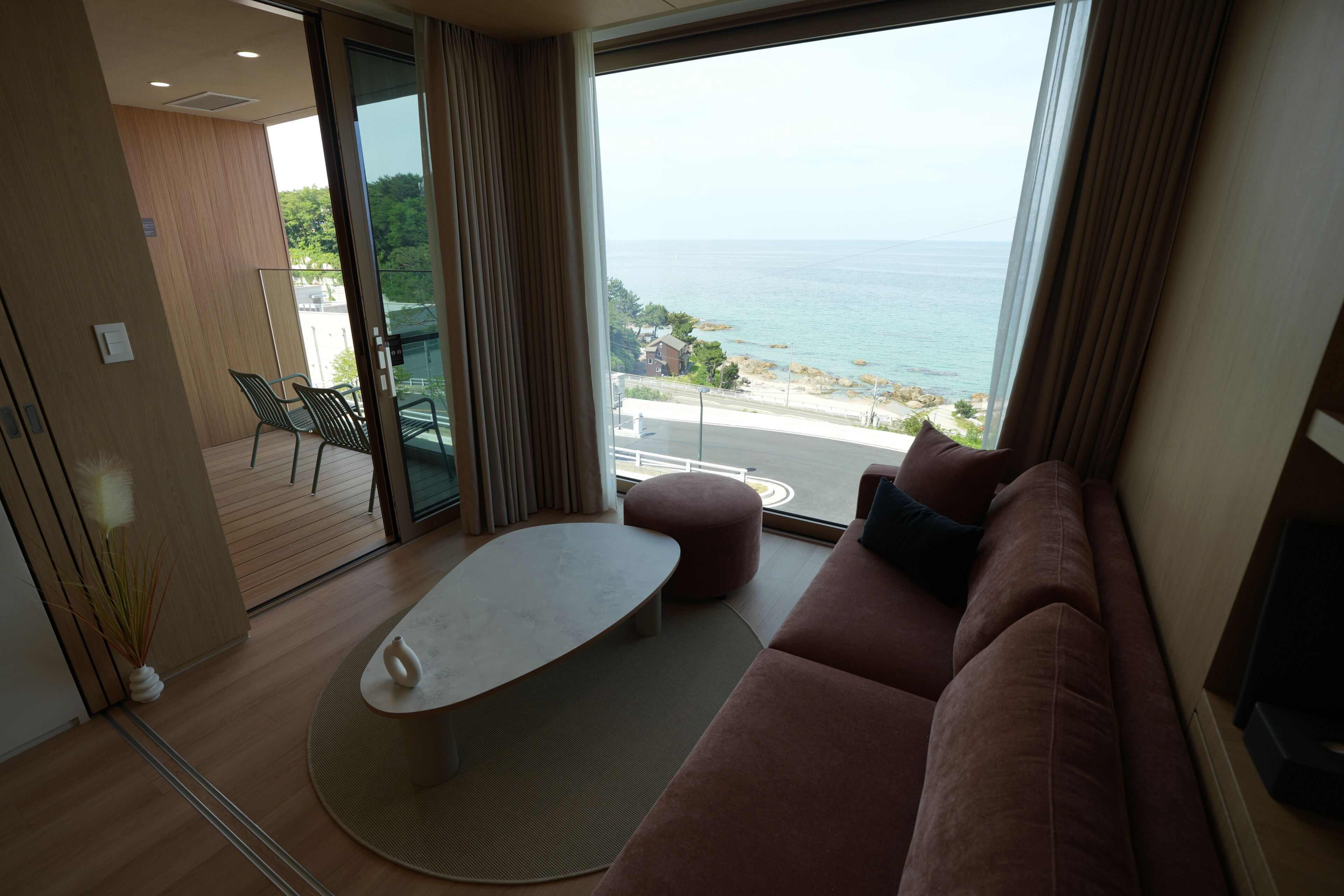 Uma sala de estar moderna com uma janela grande, um sofá, uma mesa de centro e vista para o mar.