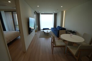 Quarto de hotel moderno com uma cama, um sofá, uma mesa de jantar e uma televisão.