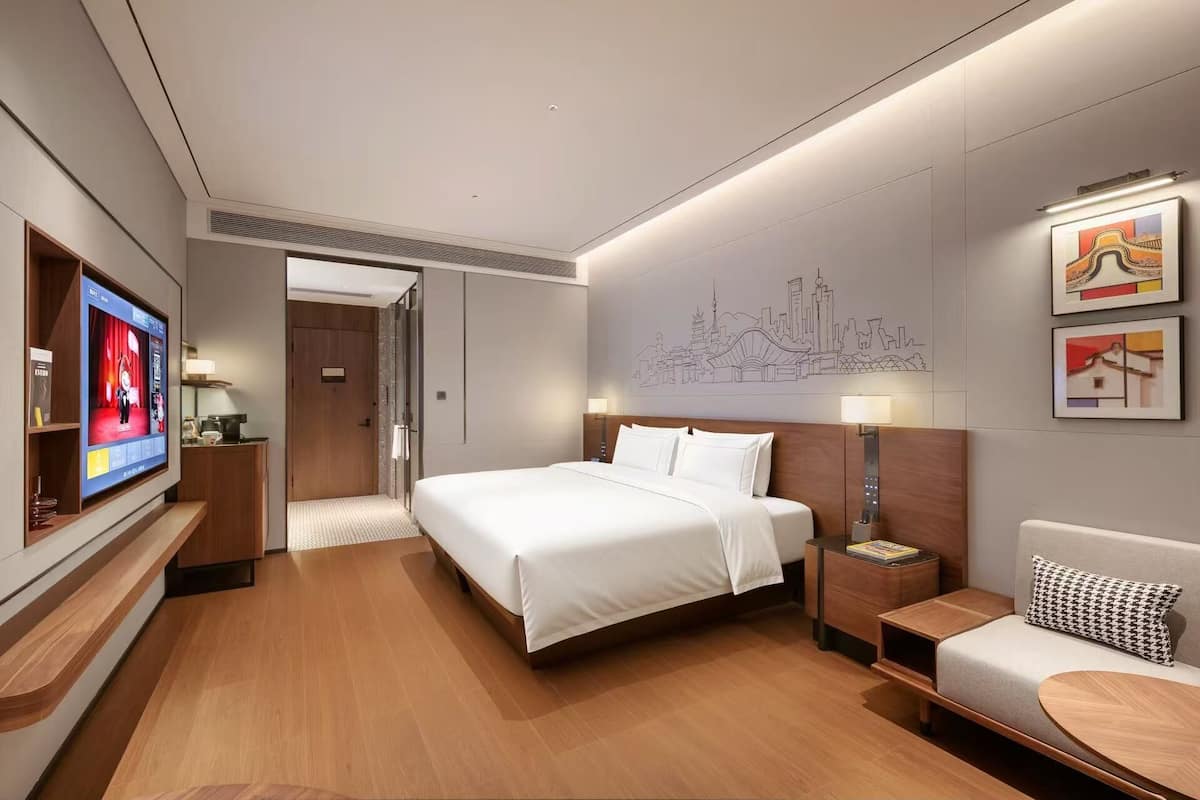 Quarto de hotel com cama, mesas de cabeceira, televisão e obras de arte nas paredes.
