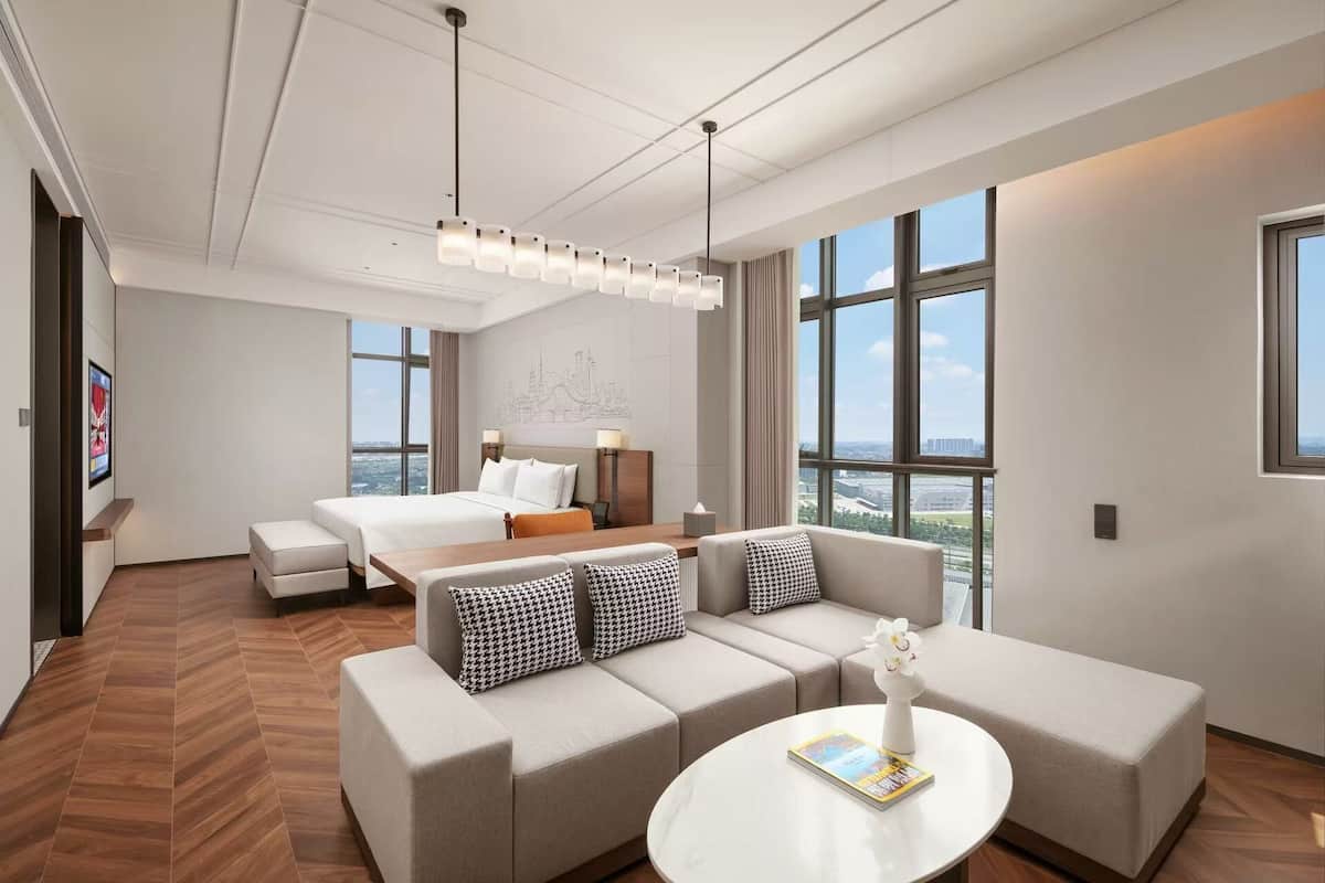 Quarto de hotel moderno com uma cama grande, um sofá, uma mesa de centro e vista para a cidade.