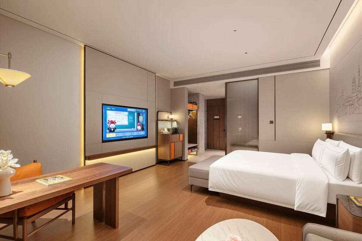 Quarto de hotel com cama, mesa de cabeceira, televisão e escrivaninha com cadeira.