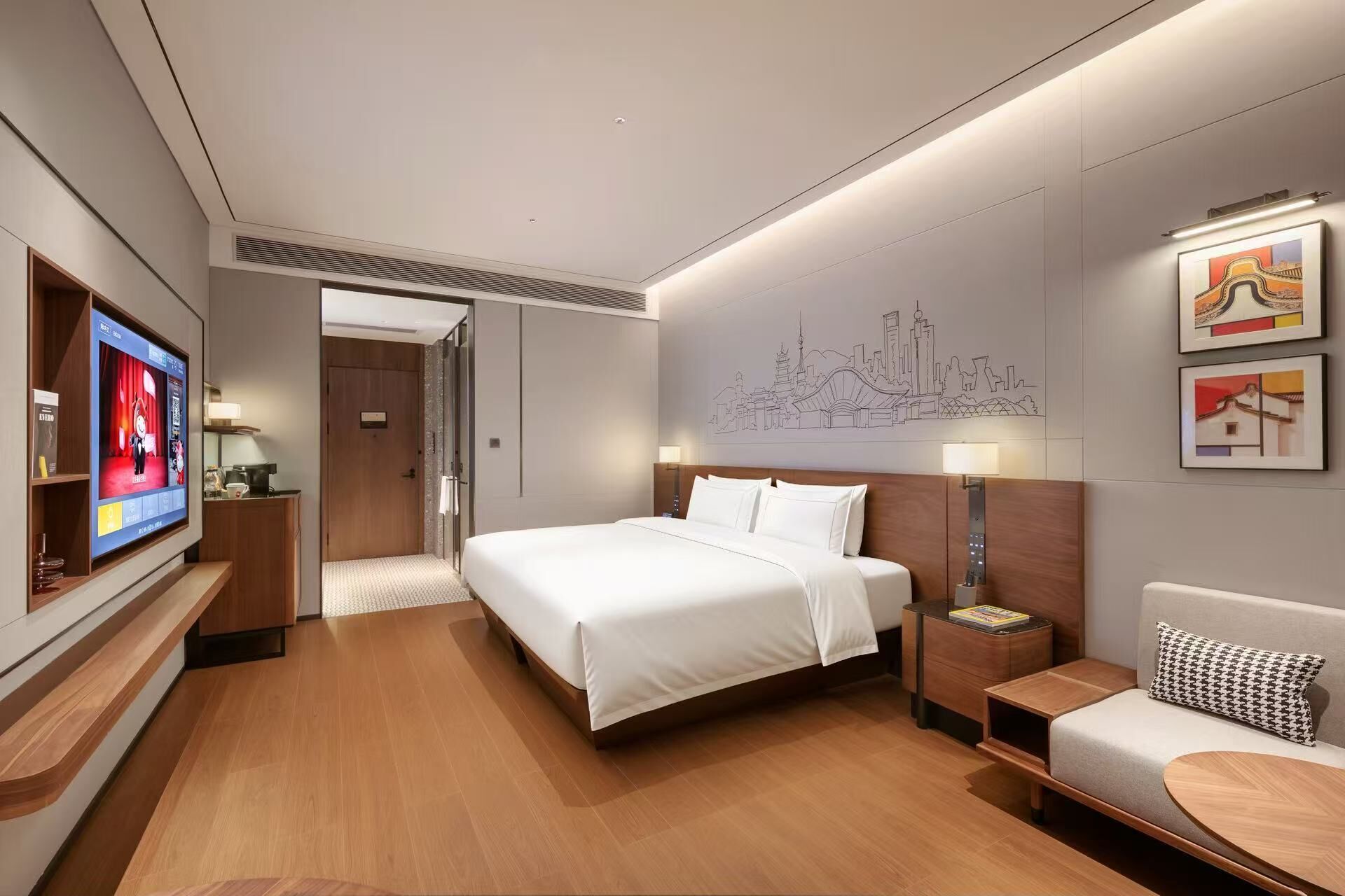 Quarto de hotel com cama, mesas de cabeceira, televisão e obras de arte nas paredes.