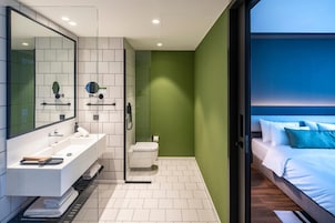 Uma casa de banho moderna com um espelho grande, azulejos brancos, cabine de duche em vidro e uma parede verde de destaque.