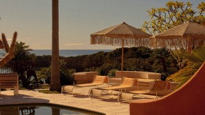 Área à beira da piscina com espreguiçadeiras, uma palmeira e vista para o oceano.