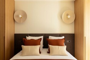 Quarto de hotel com cama, duas luminárias fixadas na parede e um guarda-roupa de madeira.