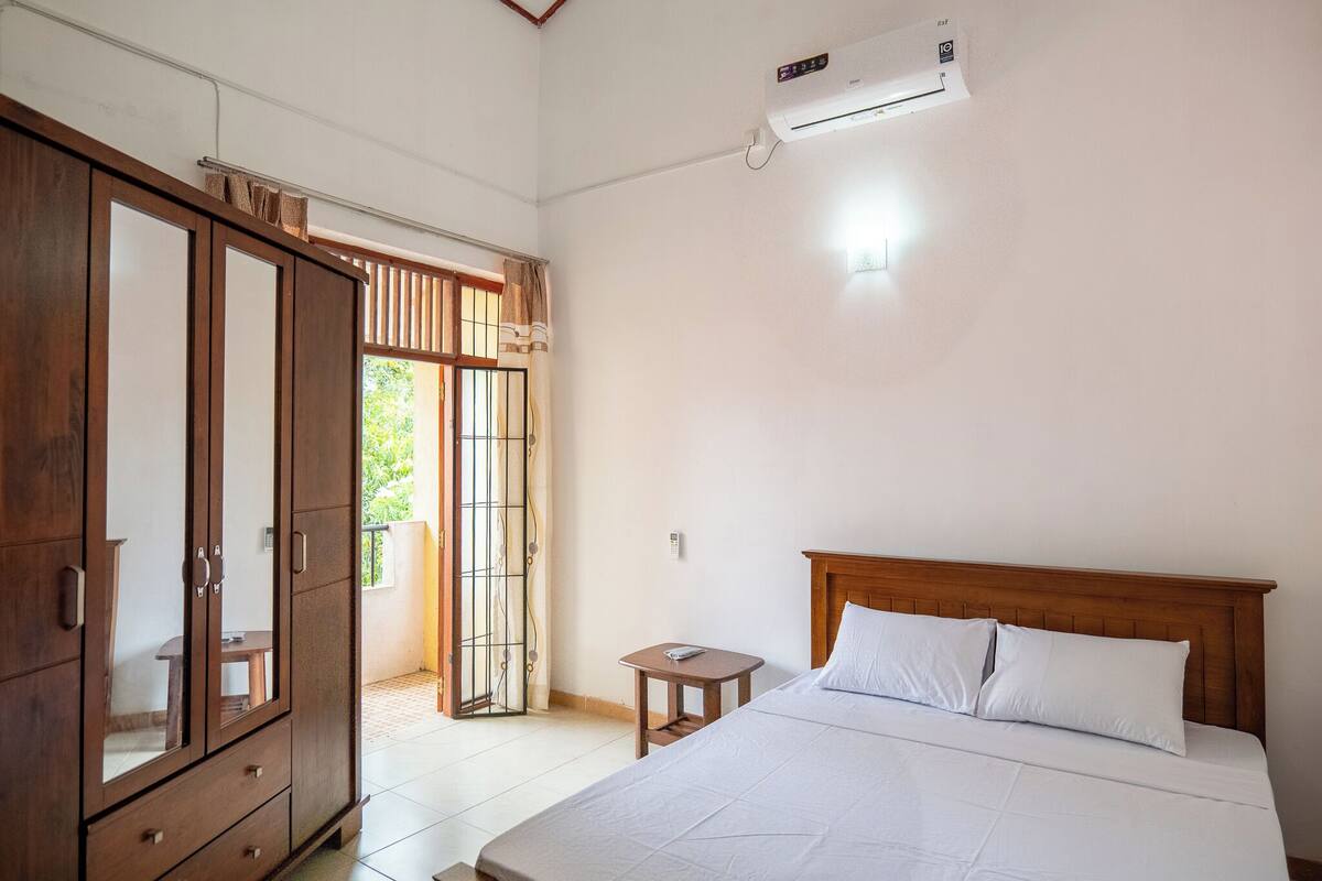 Quarto com cama, guarda-roupa, uma mesinha e ar condicionado.