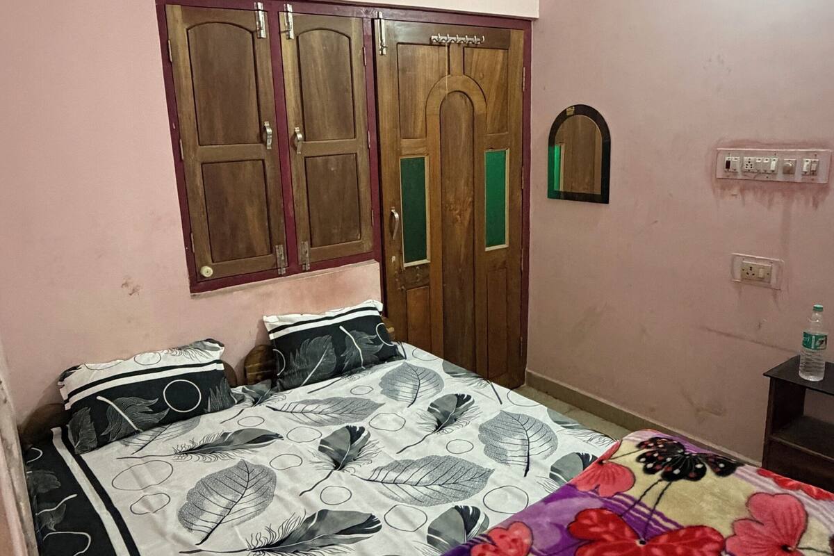 Quarto com cama, ventoinha no teto, guarda-roupa e uma mesinha com uma garrafa.