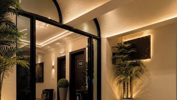 Um saguão de hotel moderno com teto curvo, uma grande planta em vaso e uma entrada bem iluminada.