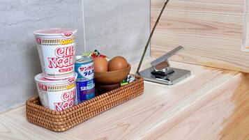 Uma superfície de madeira com uma cesta trançada contendo latas, ovos e um objeto de metal.