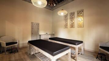 Um quarto com duas mesas de massagem de madeira, uma cadeira de vime, um banco de madeira e um lustre.