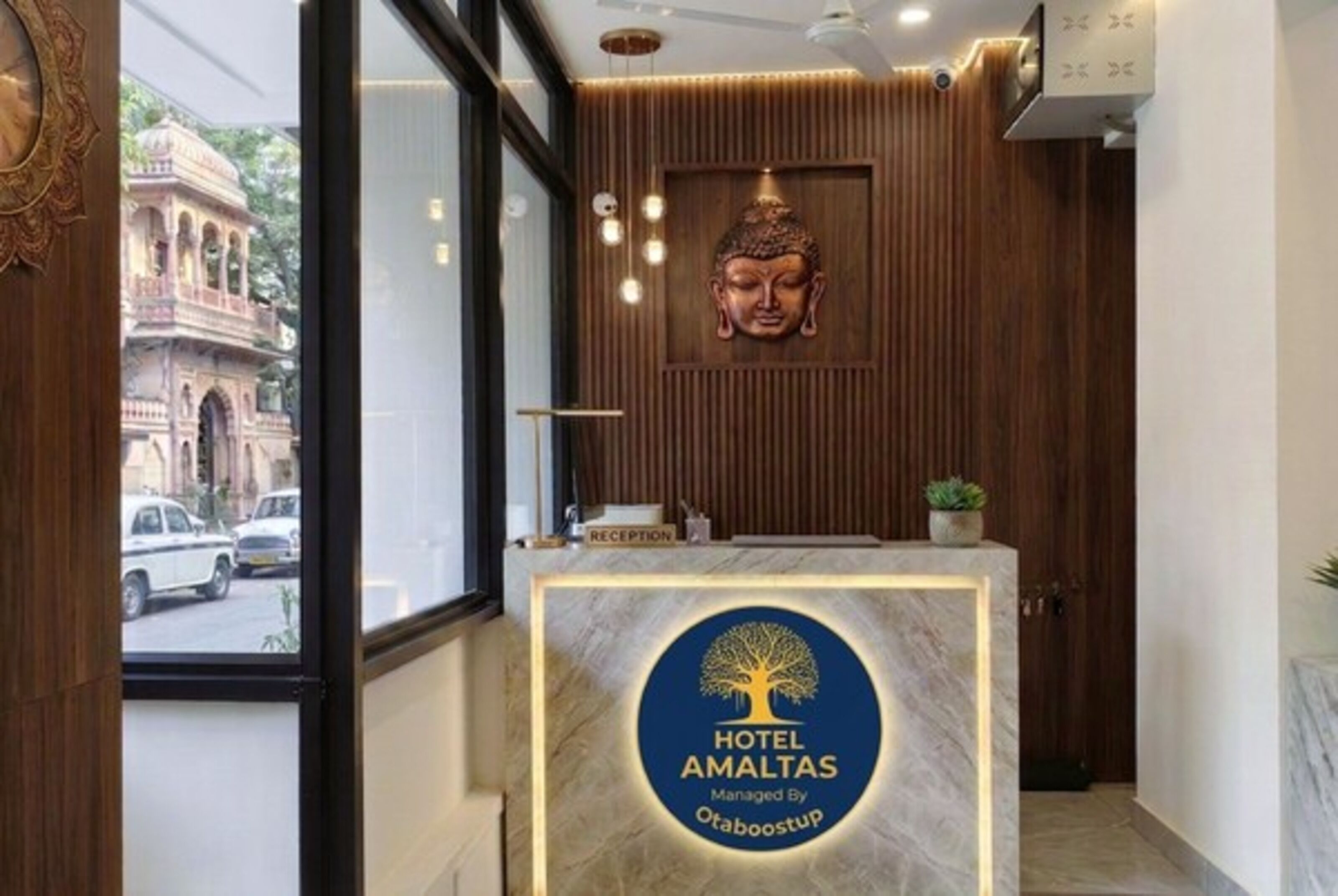 Bancada de recepção de hotel com uma estátua de Buda, placa de recepção e vista para um edifício.