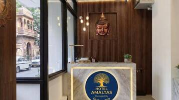 Bancada de recepção de hotel com uma estátua de Buda, placa de recepção e vista para um edifício.