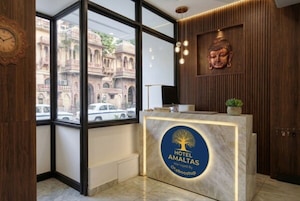 Balcão de recepção de hotel com um logotipo, uma estátua de Buda e vista para um edifício histórico através de grandes janelas.