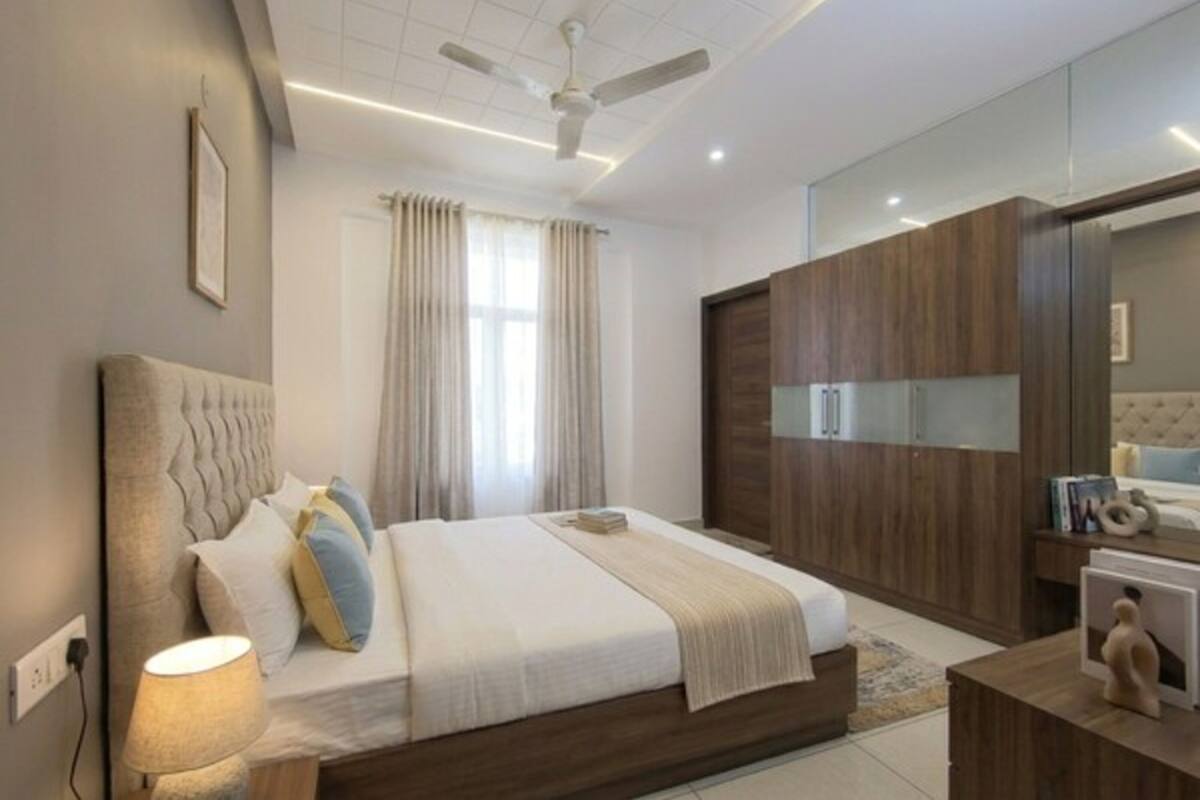 Um quarto moderno com cama, abajur, guarda-roupa e ventoinha no teto.