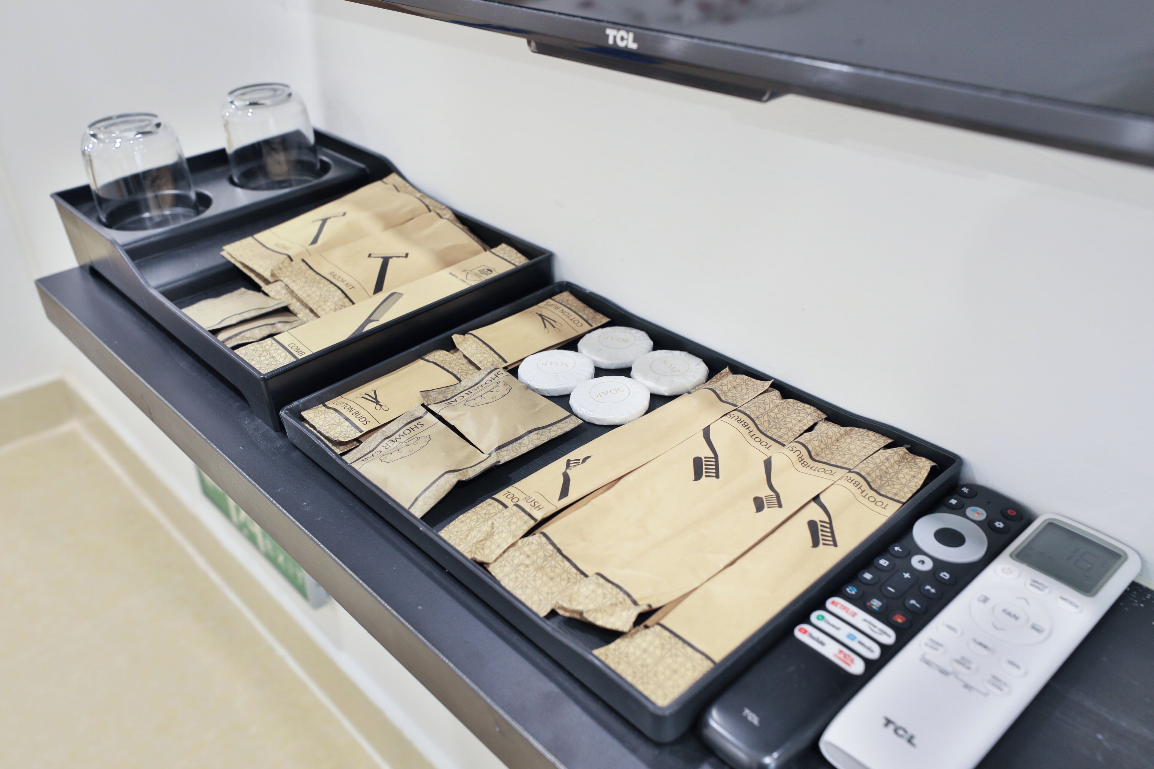 Uma bandeja preta com vários produtos de higiene pessoal e um controle remoto.