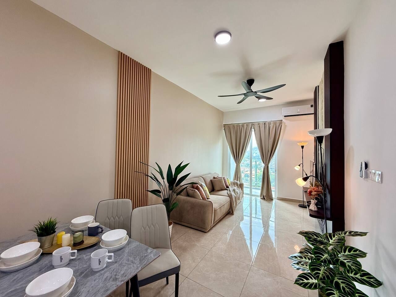 Uma sala de estar moderna com sofá, mesa de jantar e cadeiras. Há um ventilador de teto, uma janela grande com cortinas e um vaso de plantas.