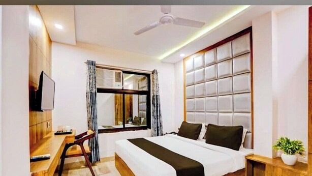 Quarto de hotel moderno com cama, escrivaninha, televisão, ventoinha no teto e janela com cortinas.