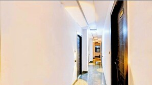 Um corredor com piso de mármore, paredes brancas e uma porta preta à direita.