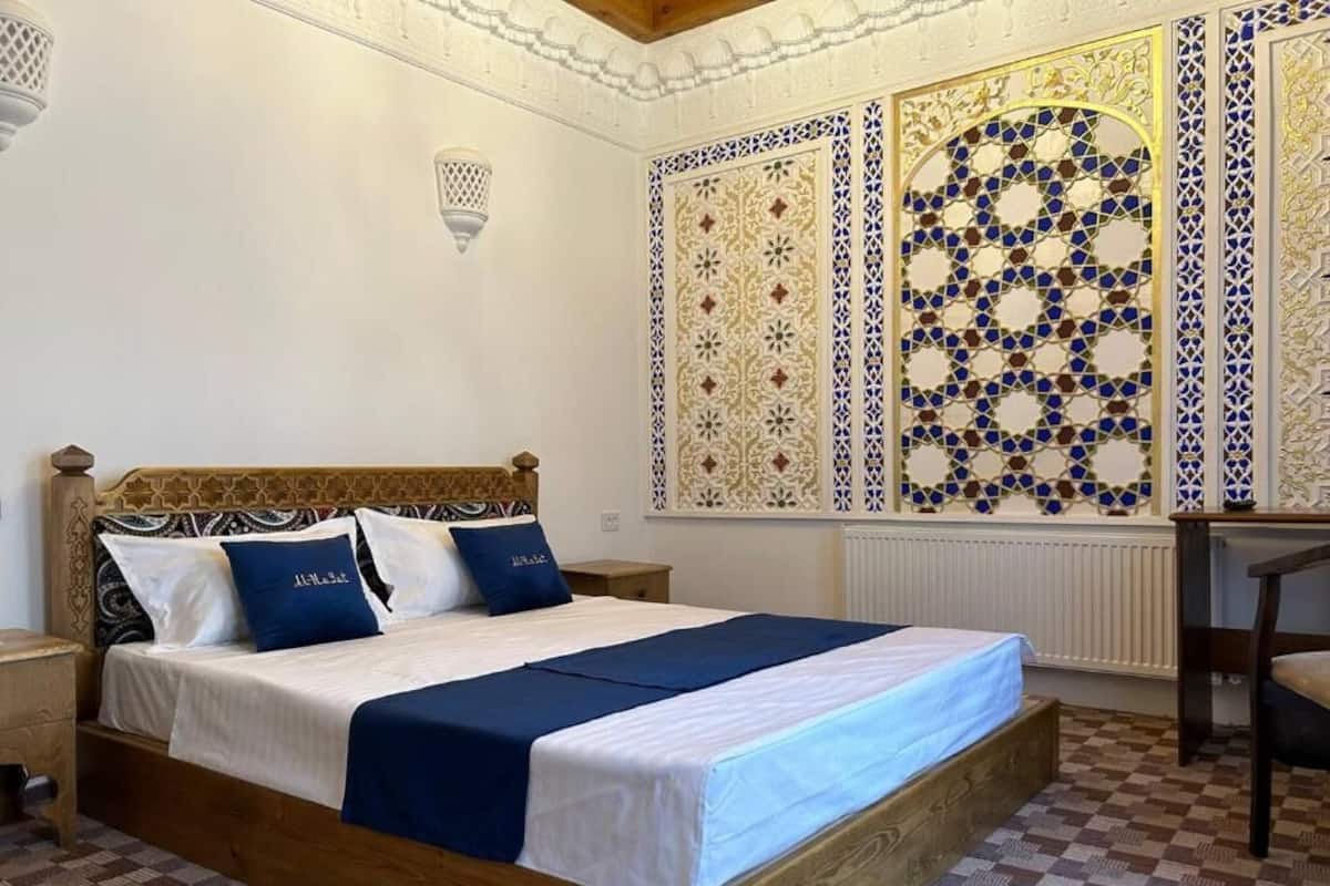 Quarto com cama de madeira, roupa de cama branca e azul, chão xadrez e detalhes decorativos nas paredes.
